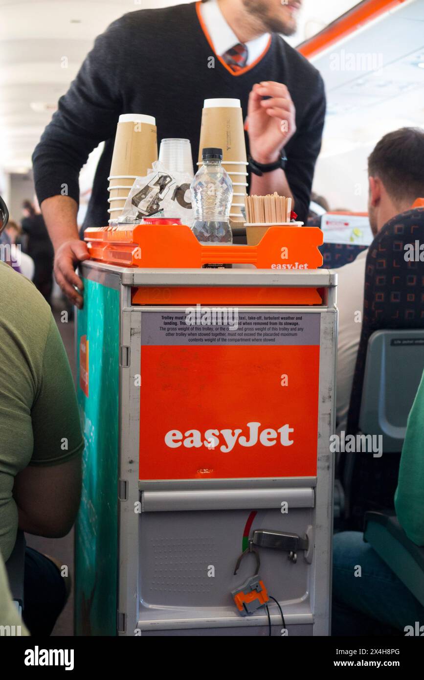 Cabin crew / air steward serves drinks and snacks to passengers from a ...