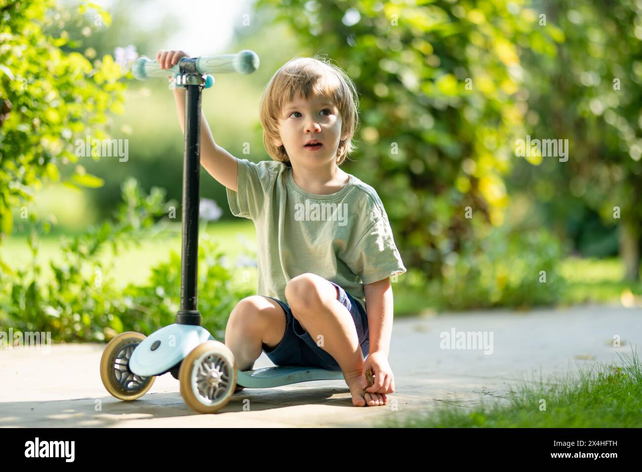 Adorable little boy riding his scooter in a back yard on sunny summer ...