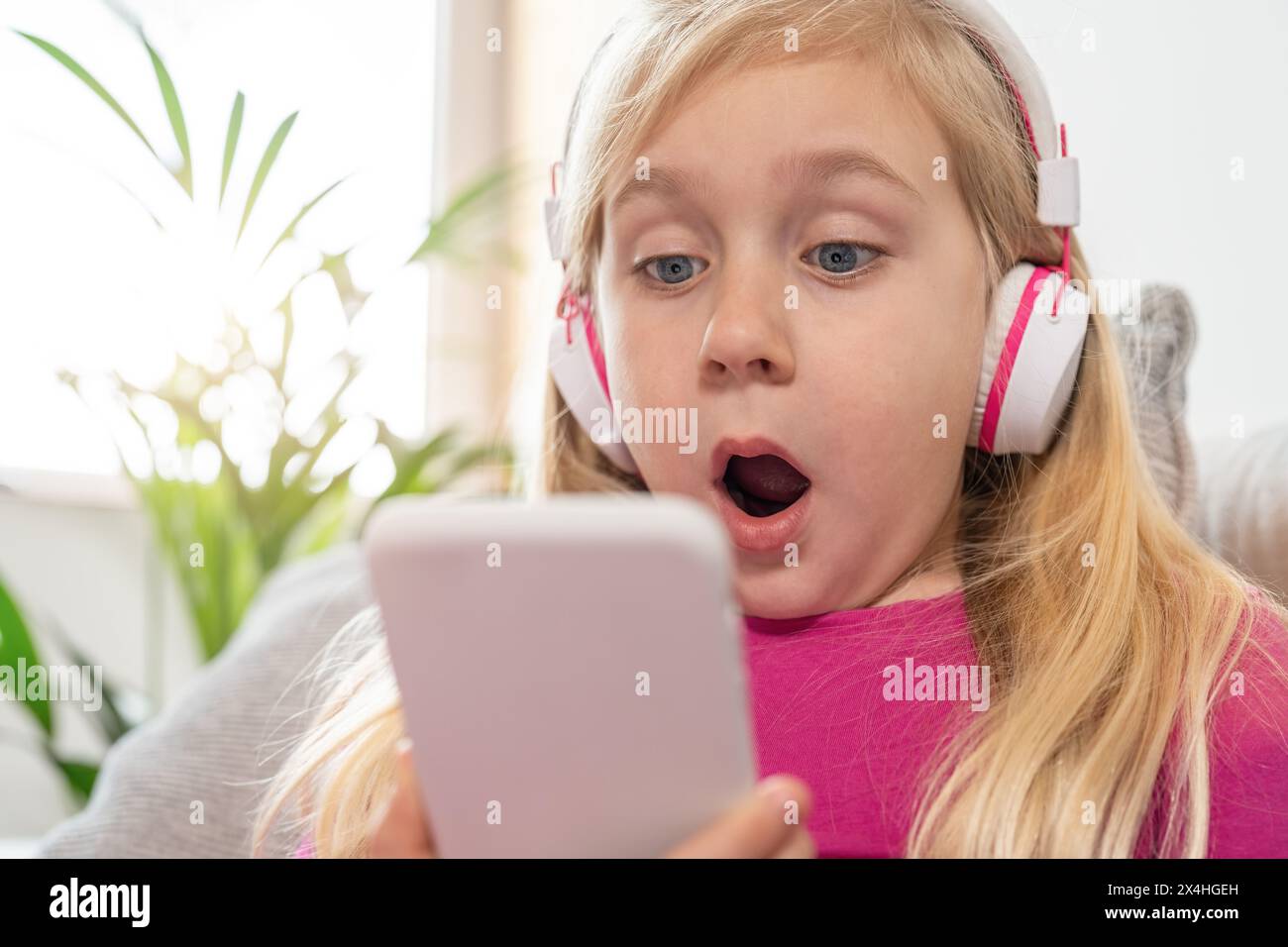 Little girl in a pink shirt and headphones is shocked and surprised ...