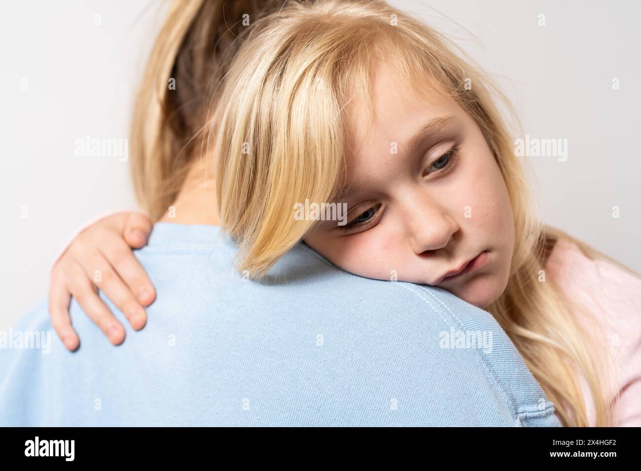 sad or sick young girl with blonde hair hugs her mother, resting her ...
