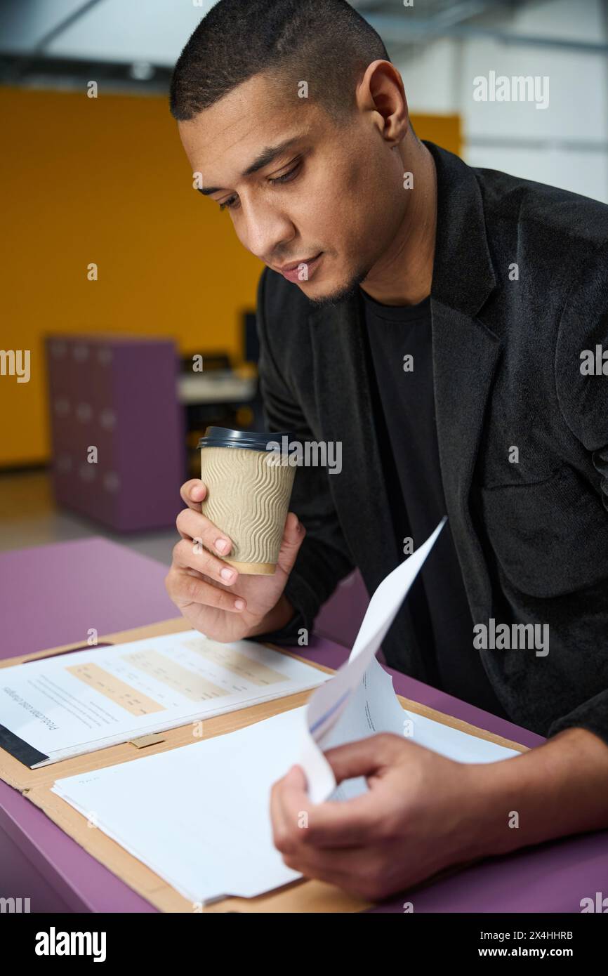 Calm male office worker checking documents and drinking coffee Stock ...