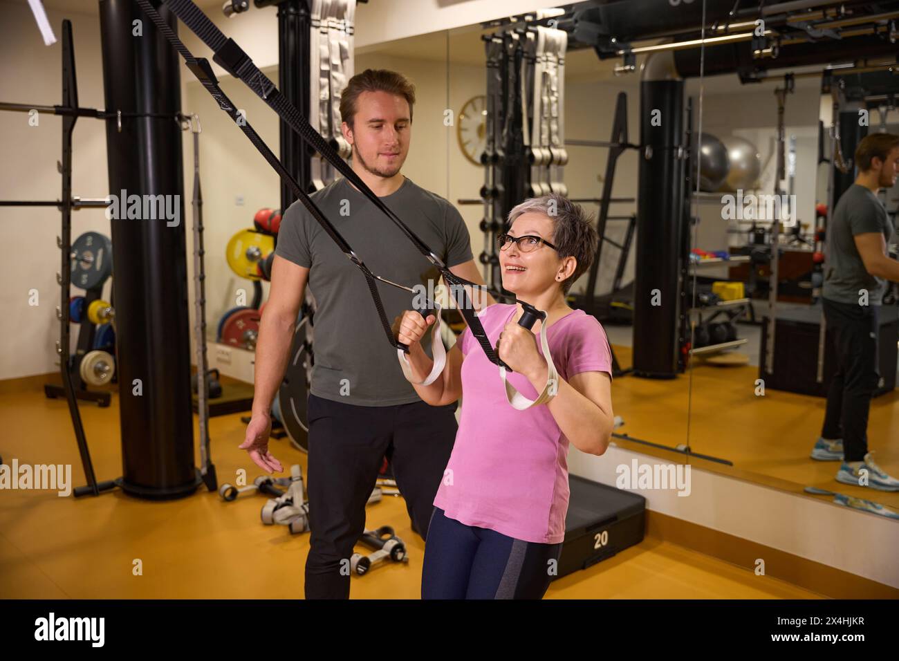 Male trainer helping mature woman doing exercise for back on hanging ...