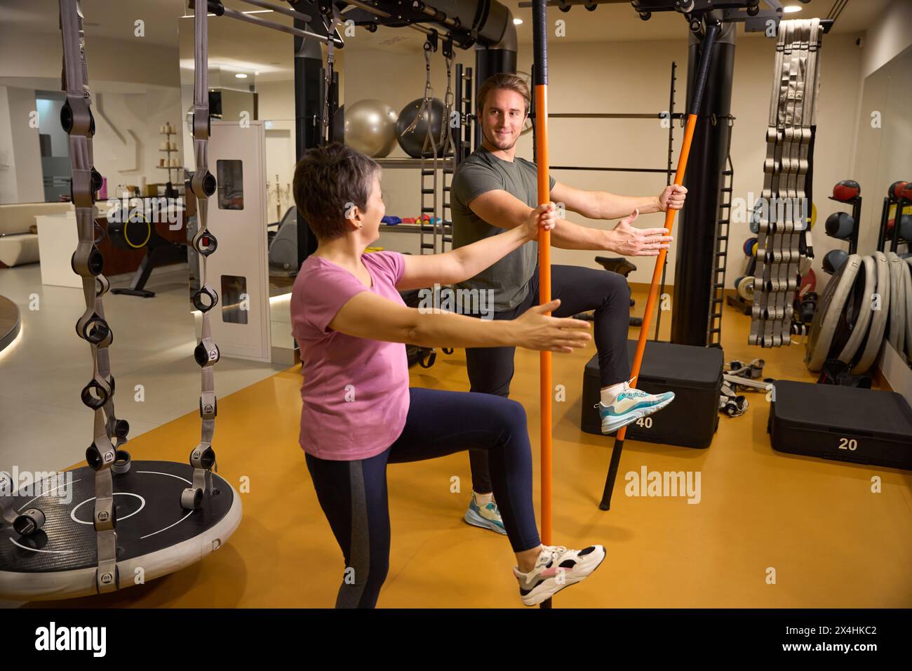 Trainer teaching mature woman doing exercise with sports sticks in gym ...