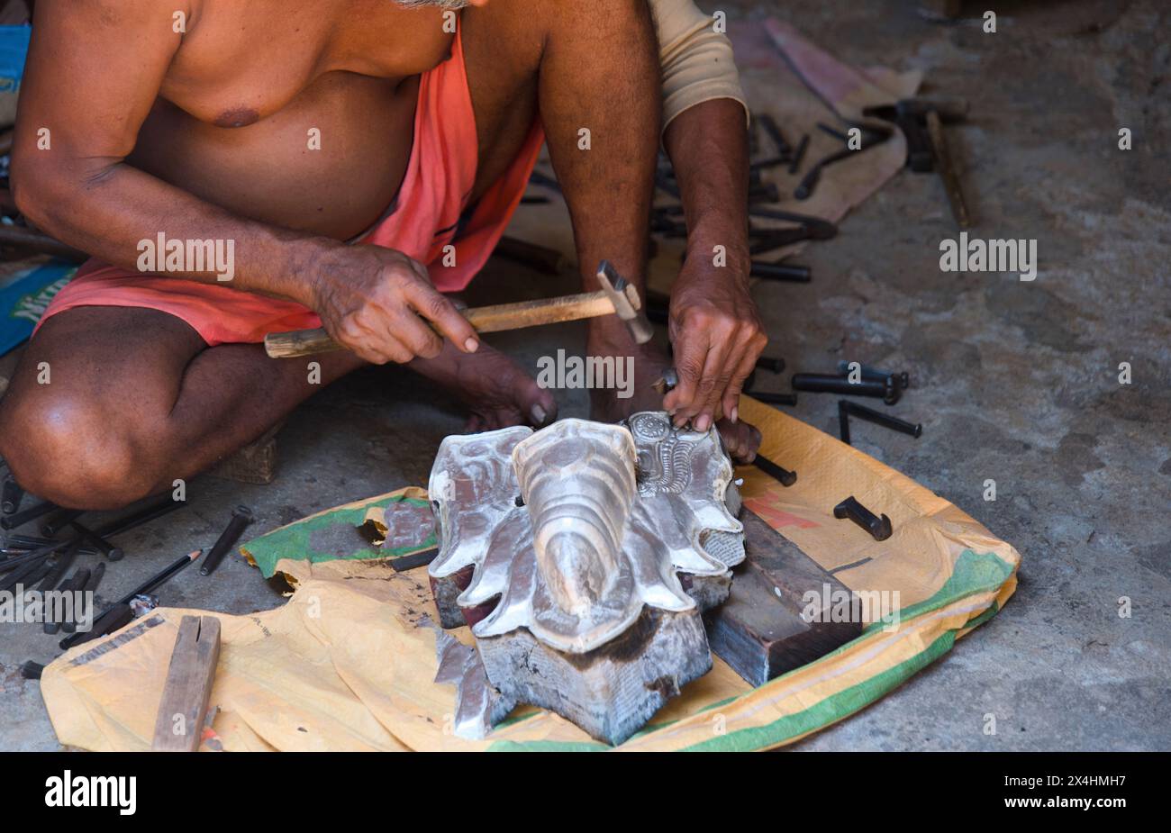 A skilled Indian craftsman meticulously works on a metal form to create ...