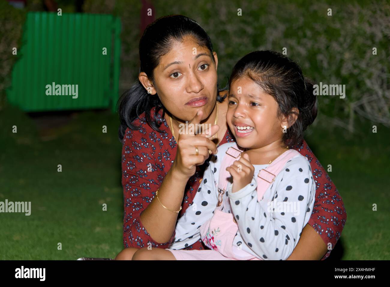 A young Indian girl cries in a lush green garden while her concerned ...