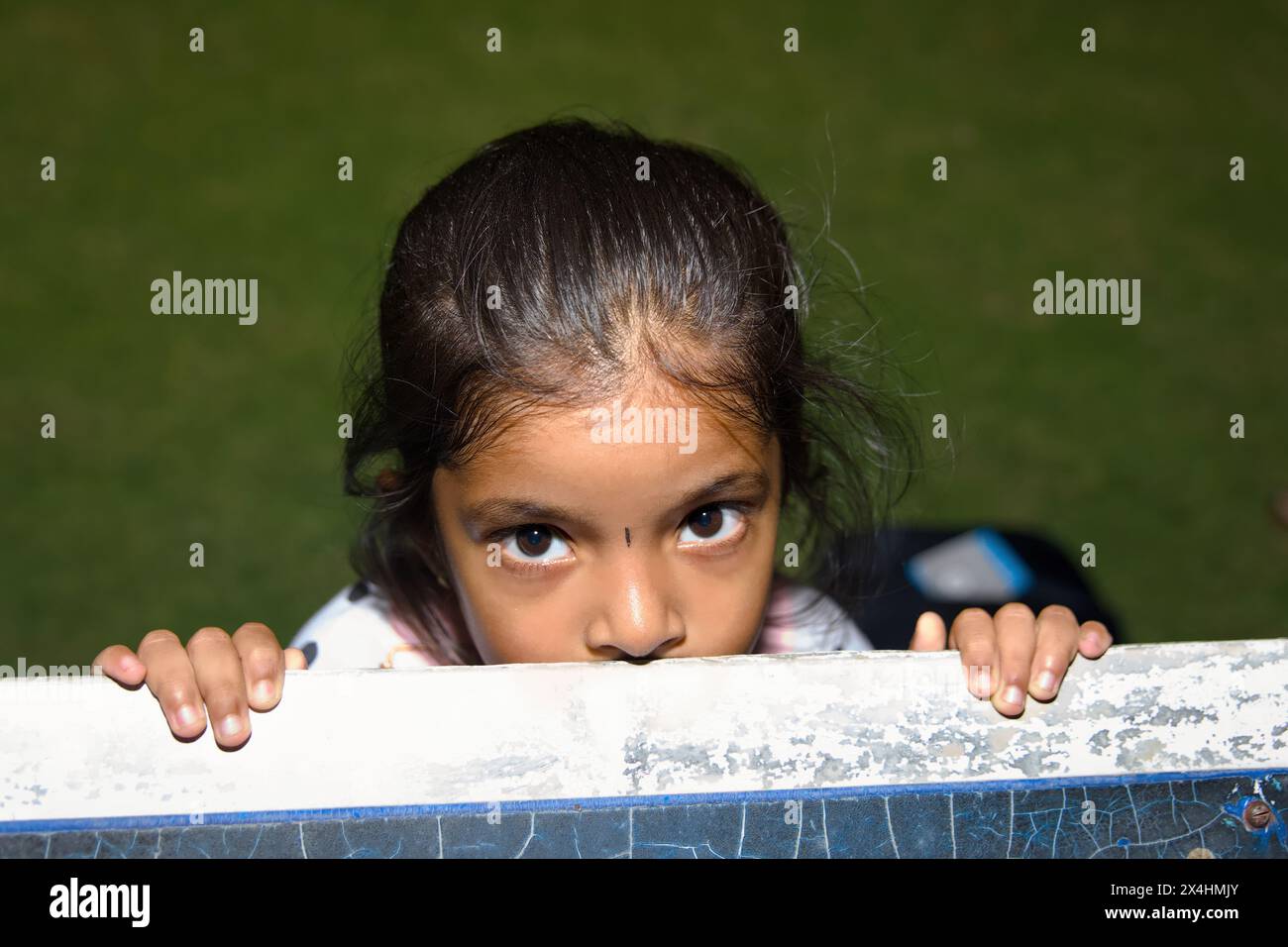 young girl playfully hides her face behind while glancing curiously at ...