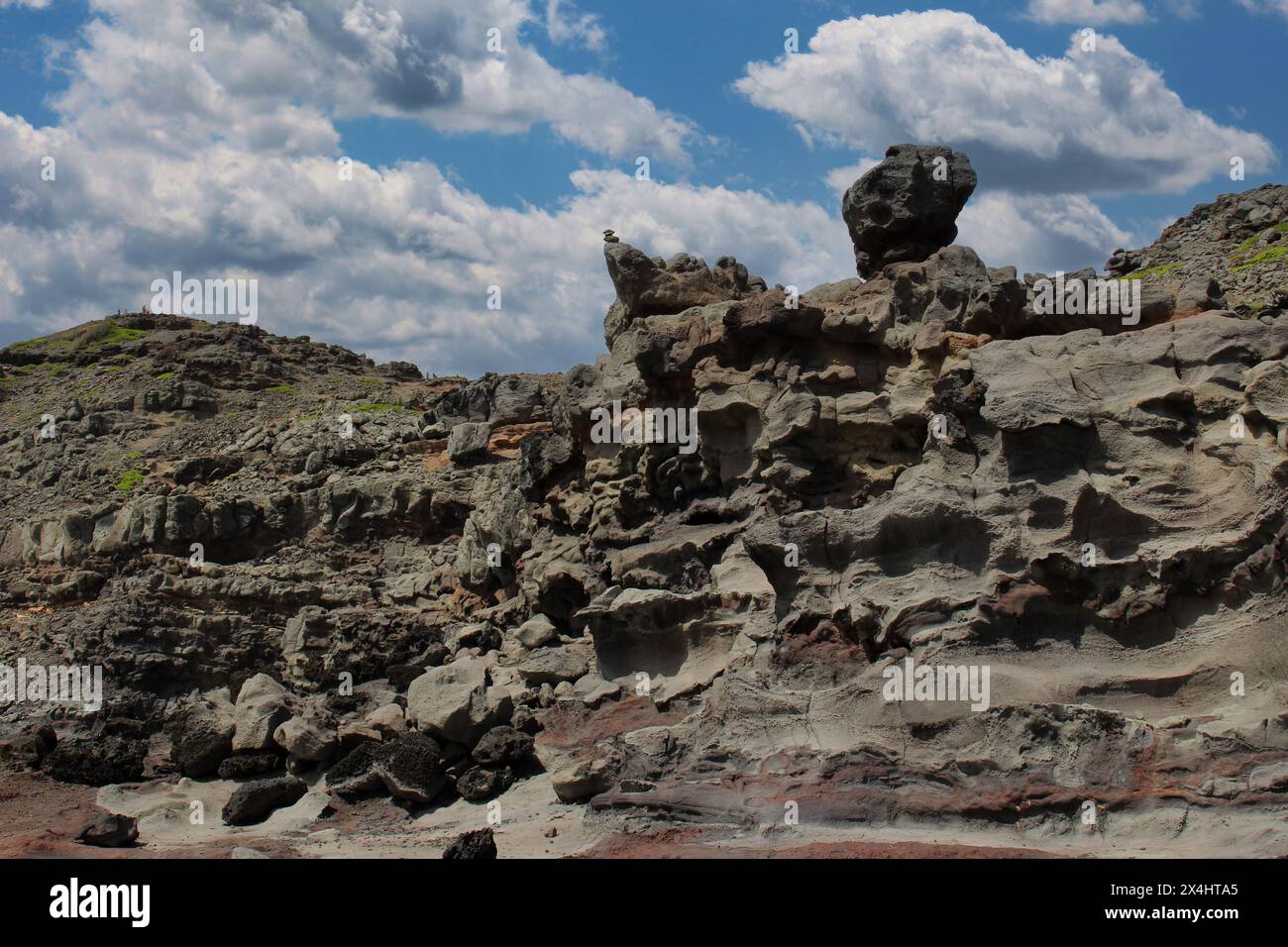 A steep hill composed of volcanic rock, with tourists at the top of the ...