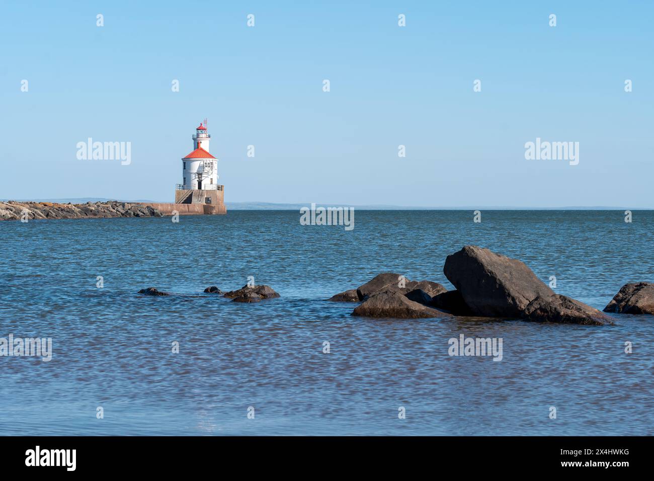 Lighthouse with red roof at the end of a pier on Lake Superior, and ...
