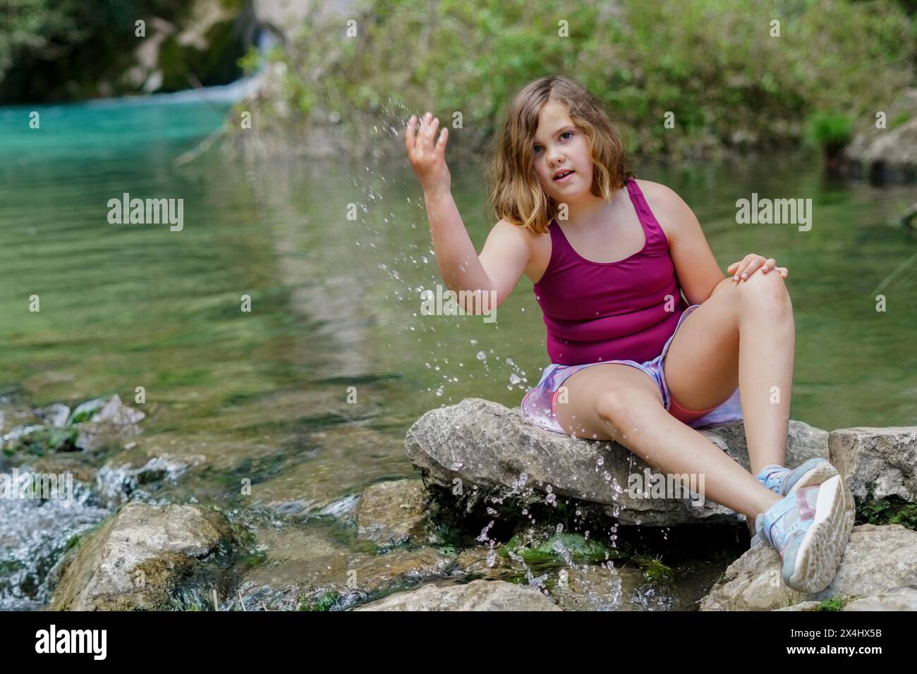 Eight-year-old girl in a red swimsuit sitting on the rocks of a ...