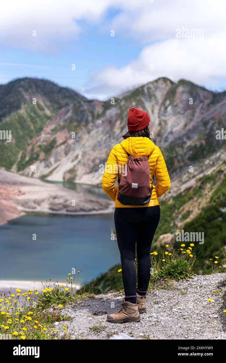 Young woman in yellow jacket standing in front of a volcano, Chaiten ...