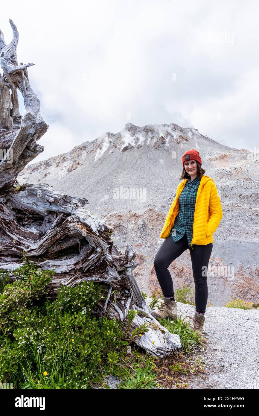 Young woman in yellow jacket standing in front of a volcano, Chaiten ...