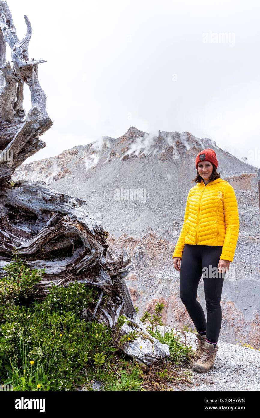 Young woman in yellow jacket standing in front of a volcano, Chaiten ...
