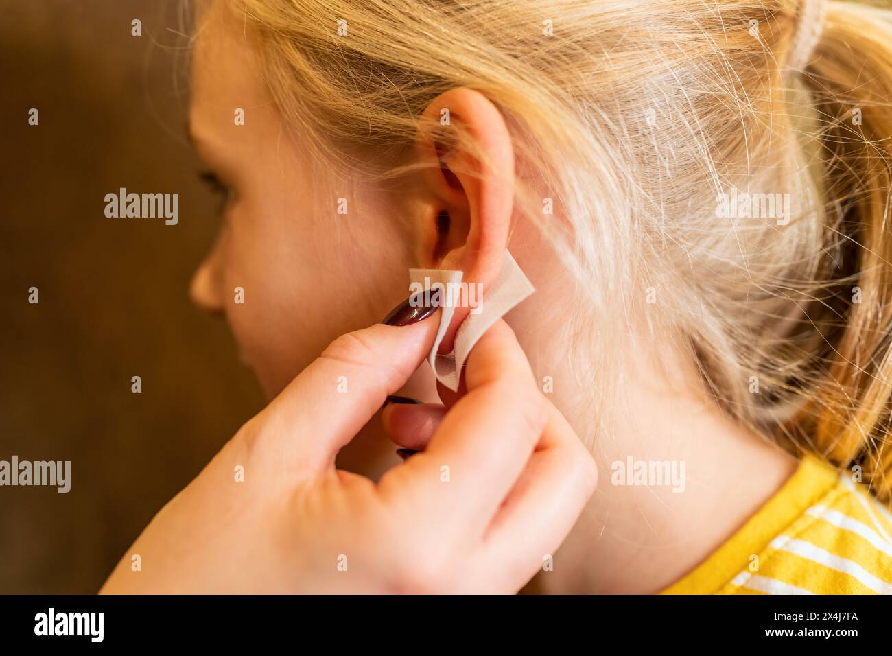 hand applying a disinfectant wipe to a young girl's earlobe bdefore ear ...
