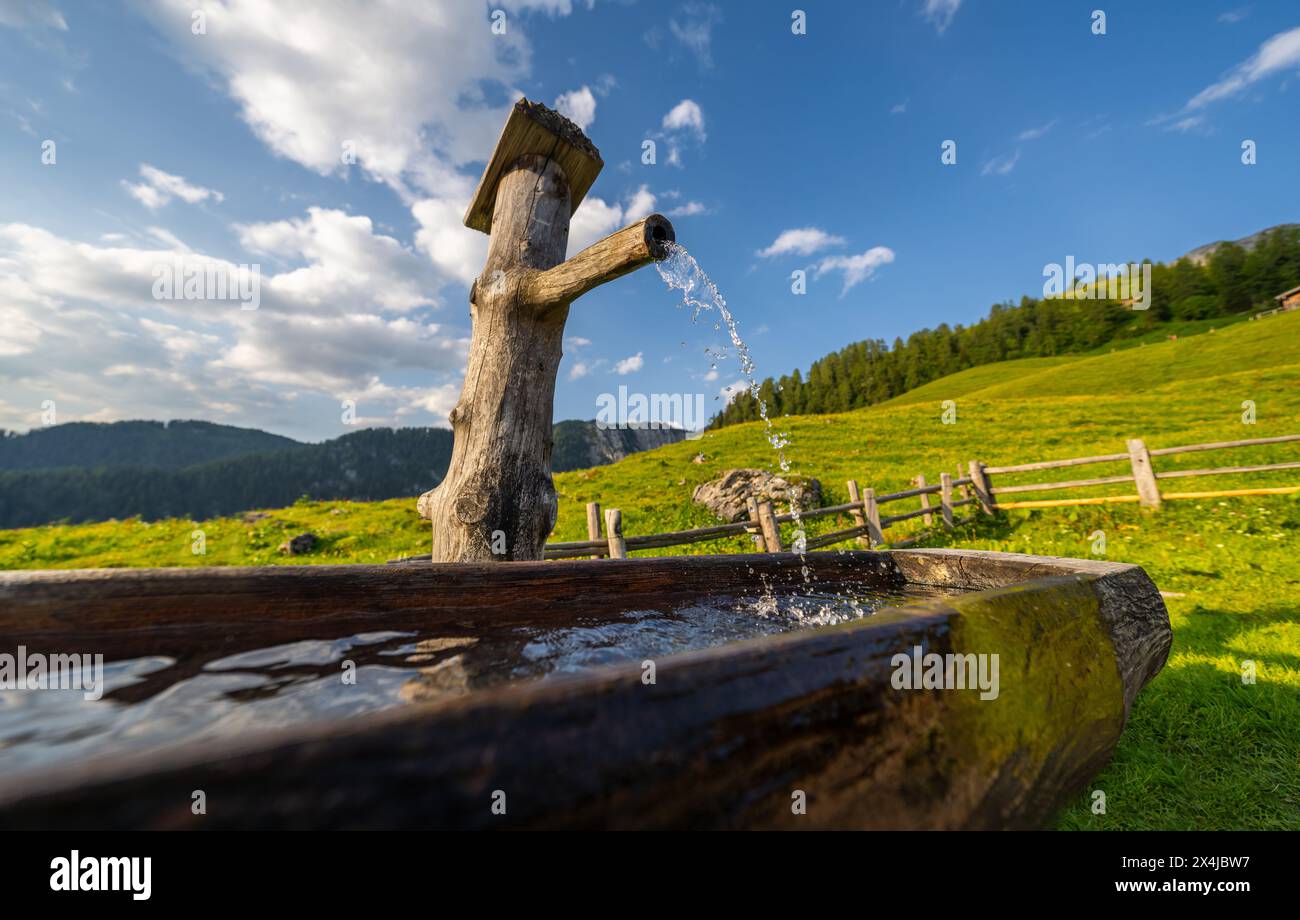 Rustic wooden trough fountain with water jet against mountain with ...