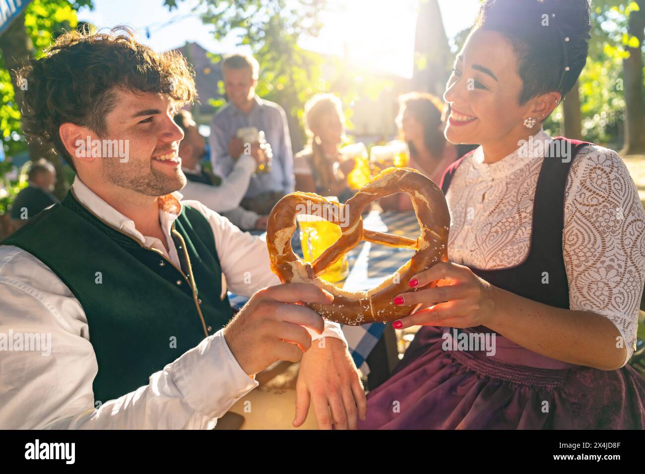 Couple in traditional German tracht holding a pretzel and smiling to ...
