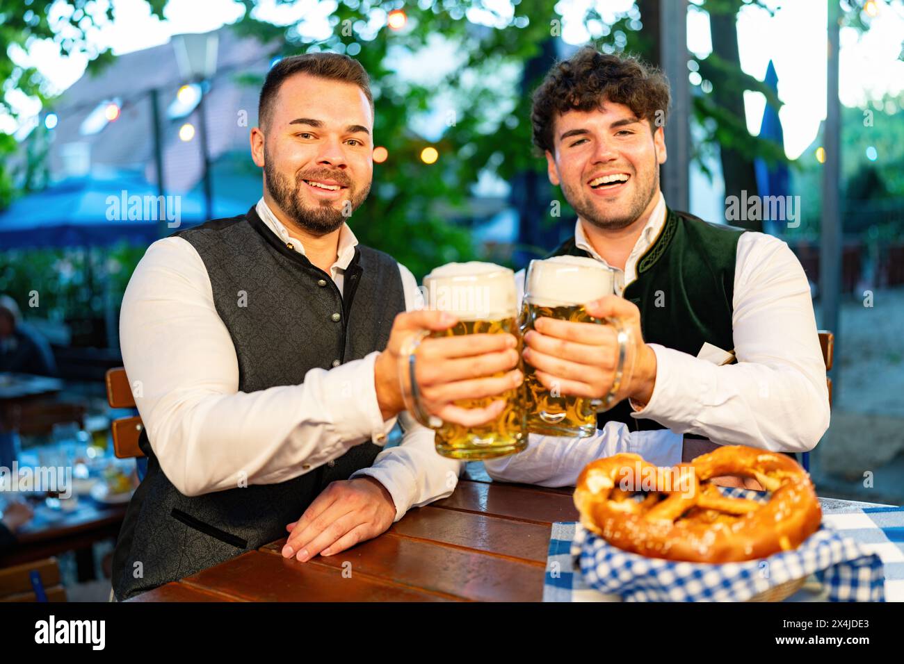 Two men in traditional Bavarian Beer garden or oktoberfest toasting ...