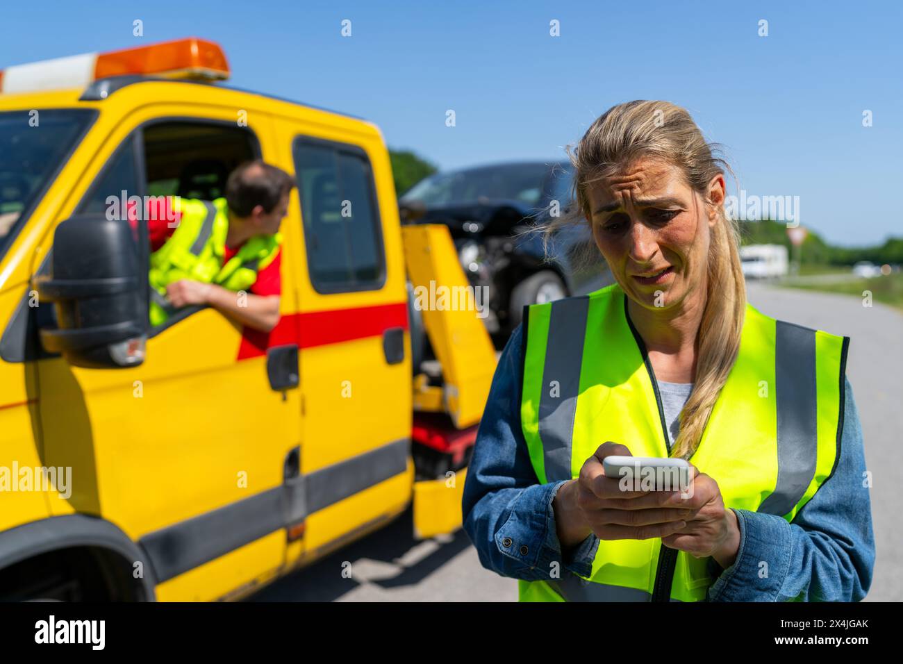 Distressed woman with smart phone in front of tow truck and damaged car ...