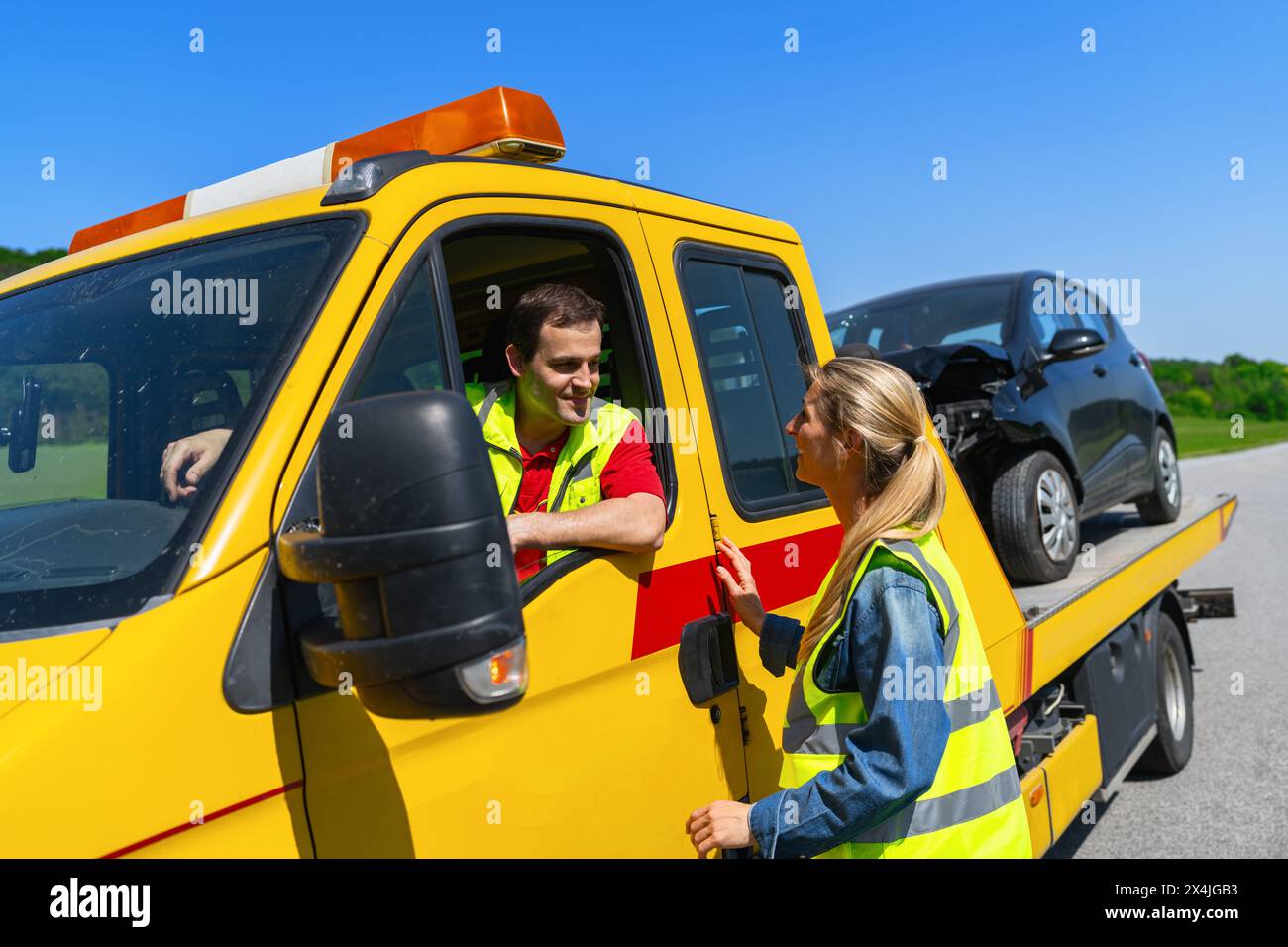 female motorist talking to tow truck driver with damaged car on flatbed ...