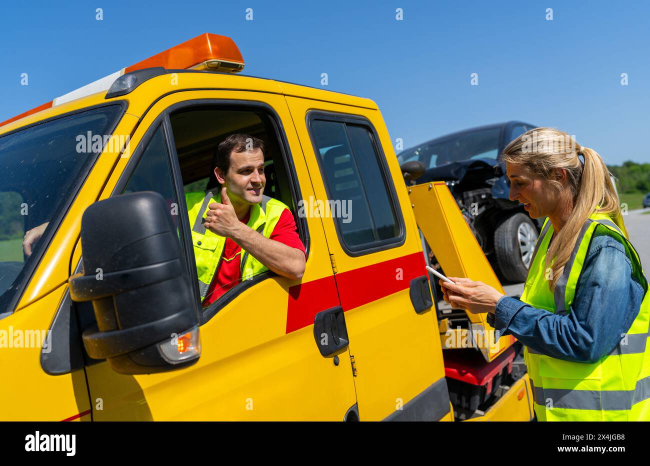 Tow truck operator giving thumbs up to woman with smart phone by ...