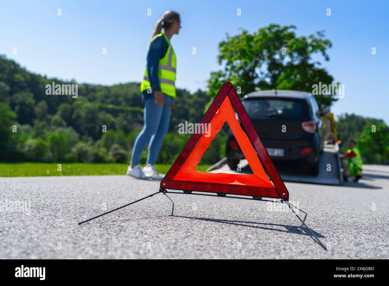 Red warning triangle on road with woman and tow truck in background ...
