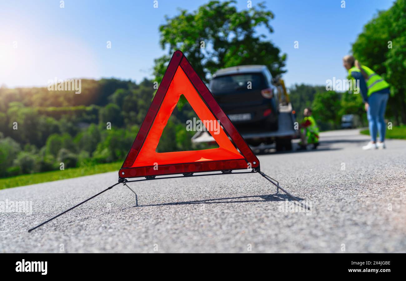 Red warning triangle on road with woman and tow truck in background ...