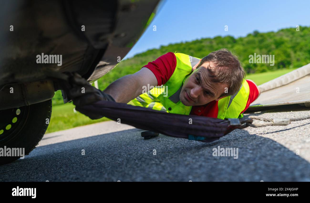 Tow Truck Worker Inspecting A Car Underneath After An Accident To