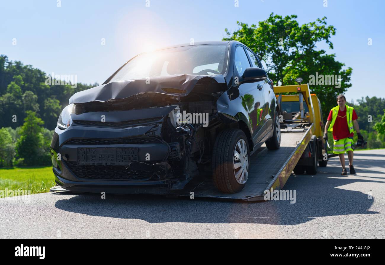 Damaged car being towed onto a flatbed tow truck with operator walking ...