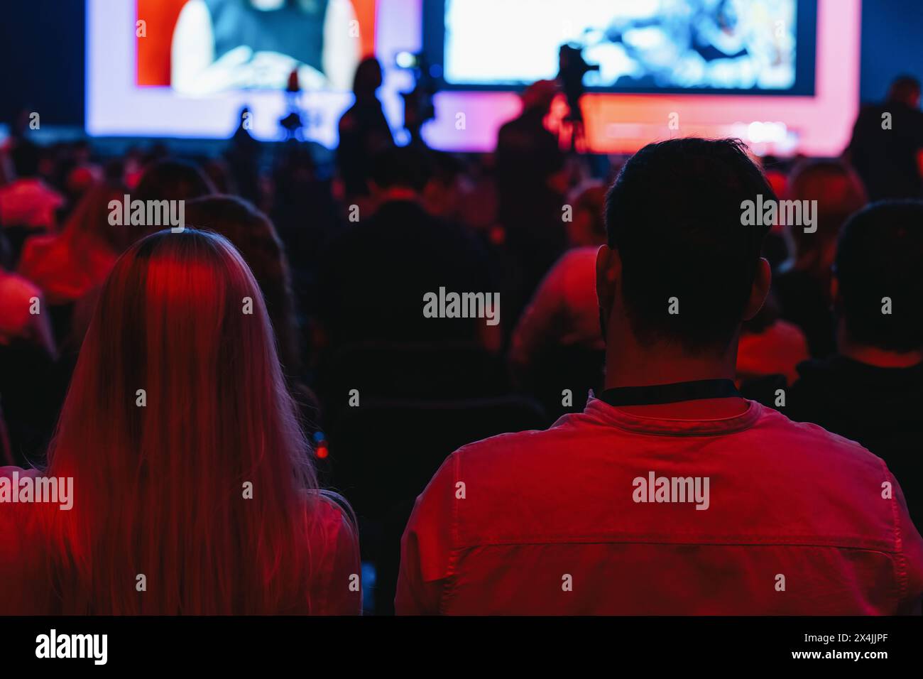 Rear view of an audience at a conference with stage lights and a ...