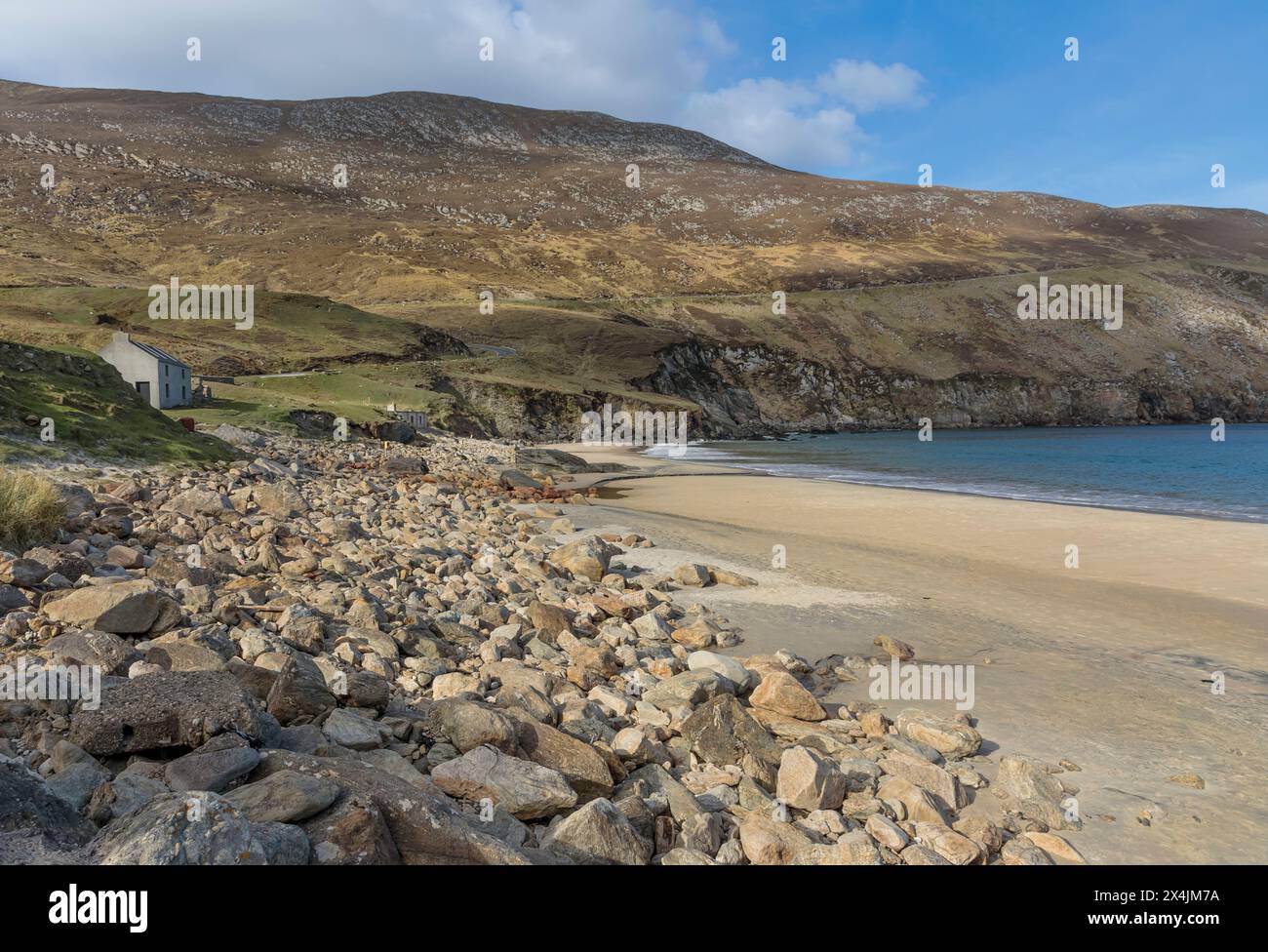 Stoney and sandy beach with a small house and a blue sky with a ...