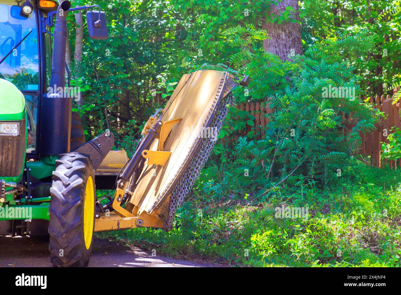 Municipal service tractor with mower cutting grass branches on both ...