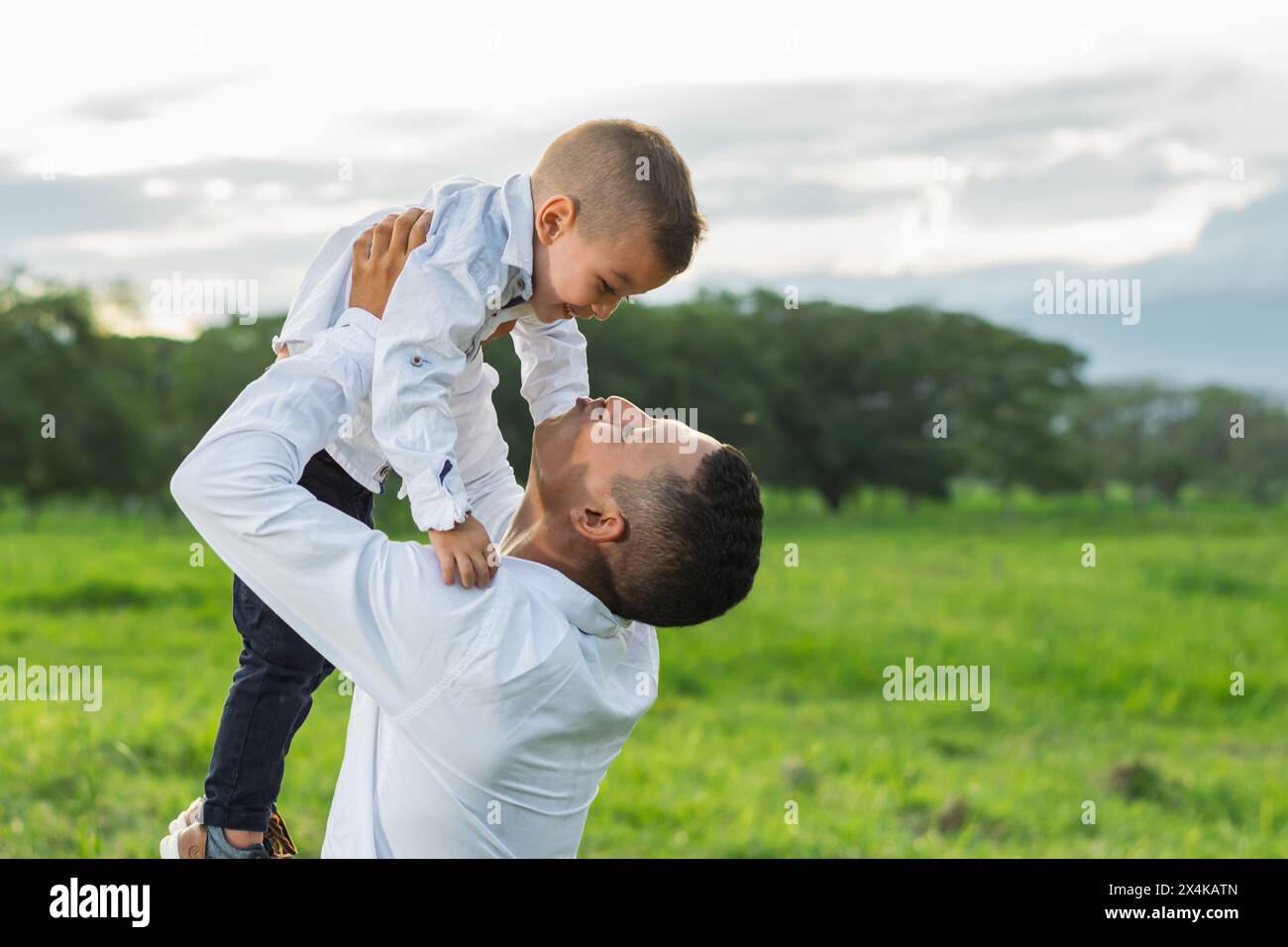 young latin father lifting his young son with his hands. pulling him up ...