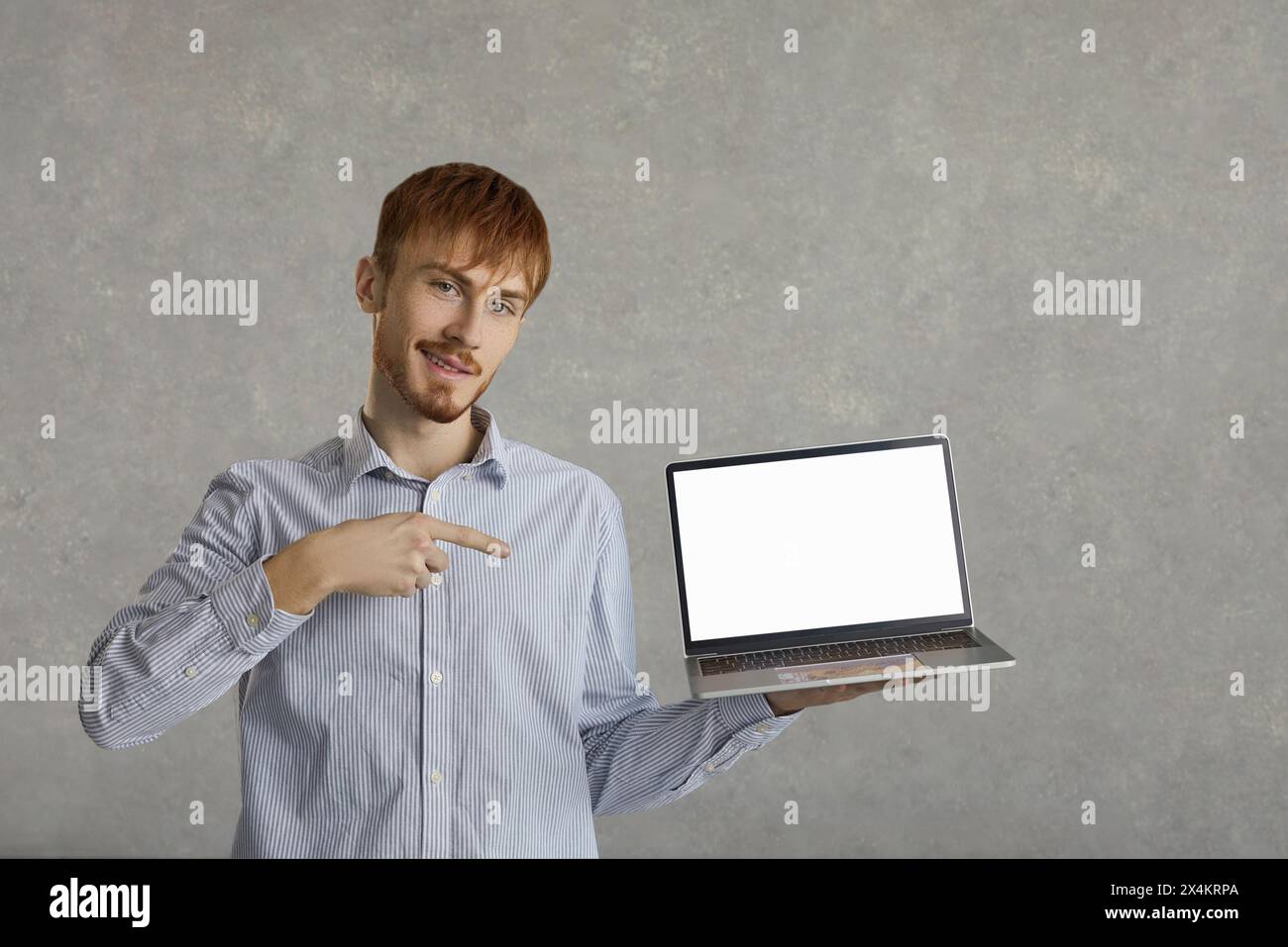 Portrait of positive young man holding laptop with blank white screen ...