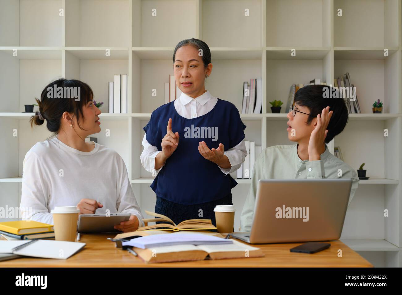 Mature professor explaining something to her students in library at ...