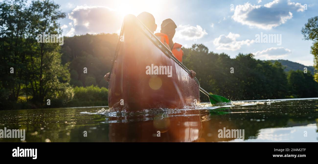 Back view of three people in a canoe paddling on a river, highlighted ...