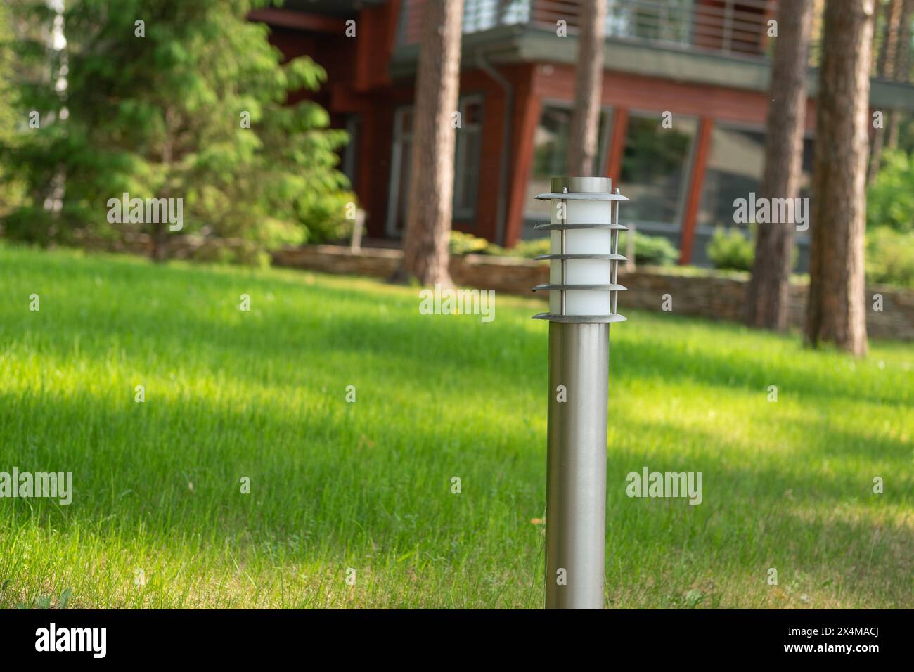 A tall, elegant silver lamp post on a vibrant green lawn near a red ...