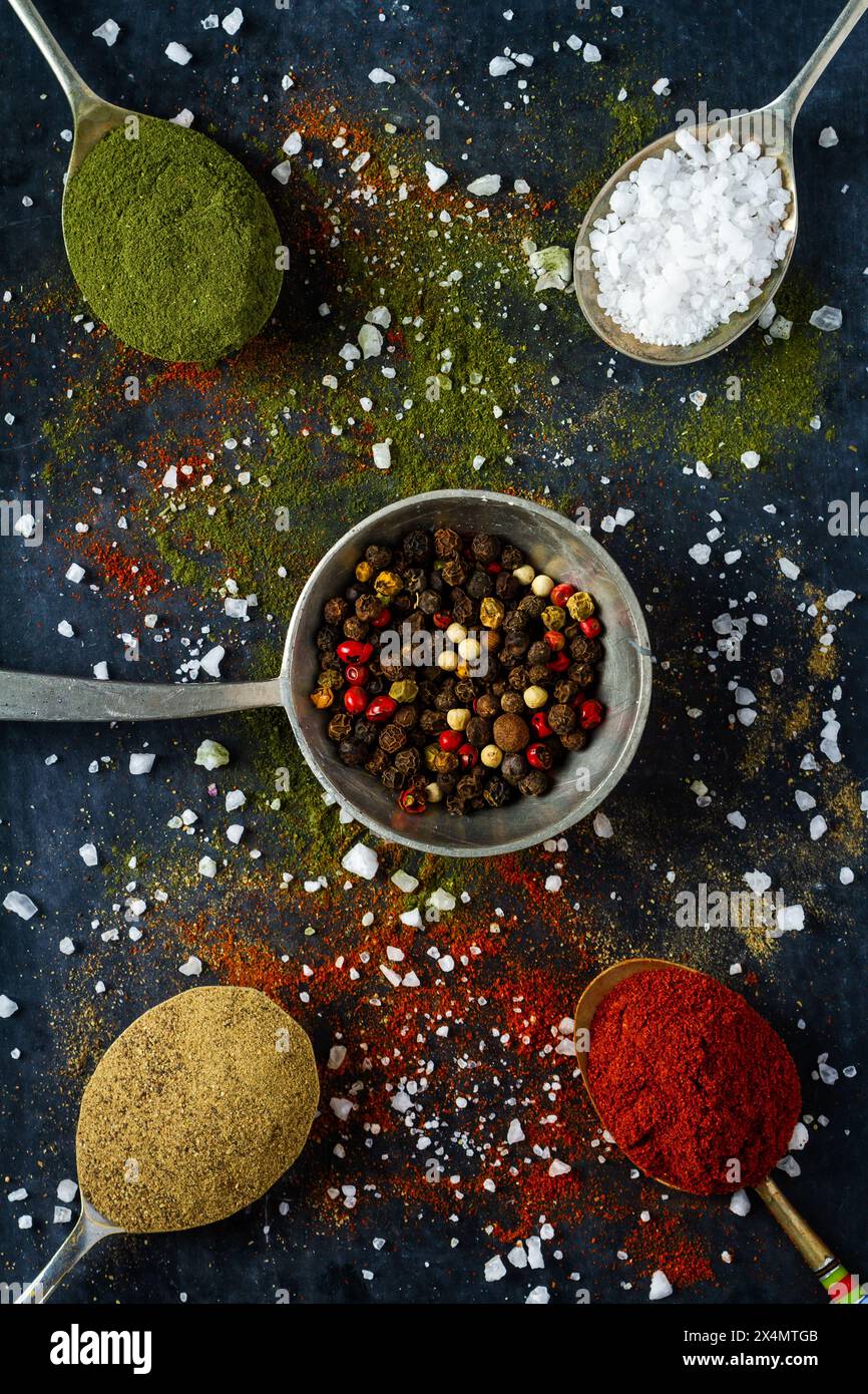 Spoons with spices and salt on black background sprinkled with ...