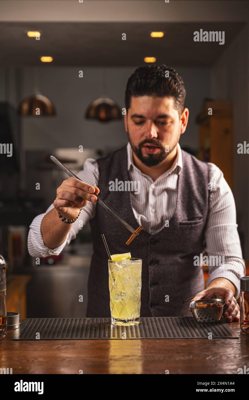 Professional male bartender meticulously adds garnish to a crafted cocktail on a bar counter ...