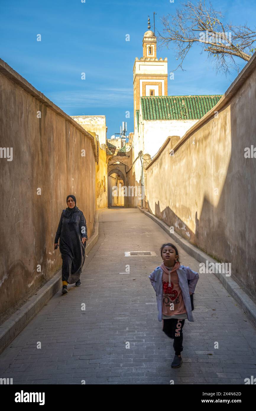 A girl and her mother stroll through a sunlit alley in Fez medina Stock ...