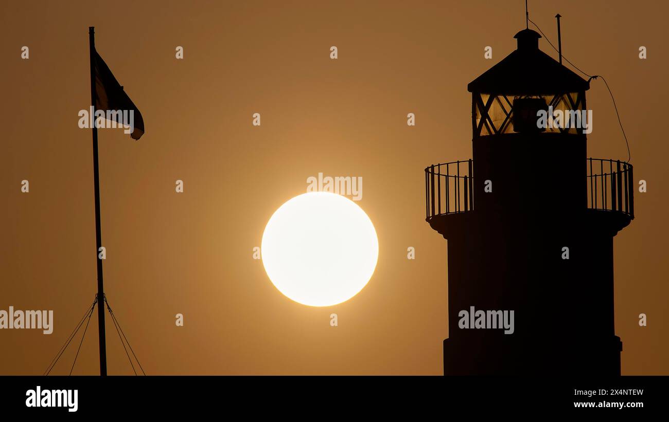 Silhouette of a lighthouse in front of an Orange coloured sky at ...