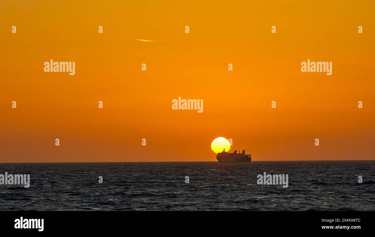 The setting sun forms the backdrop for a ferry sailing on the sea in ...