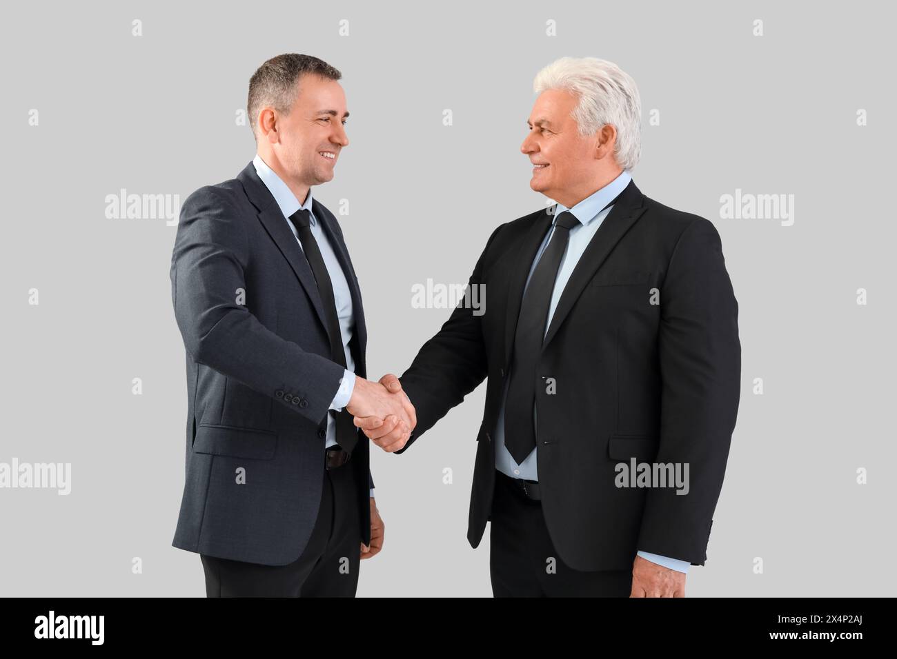 Mature brothers in suits shaking hands on grey background Stock Photo ...