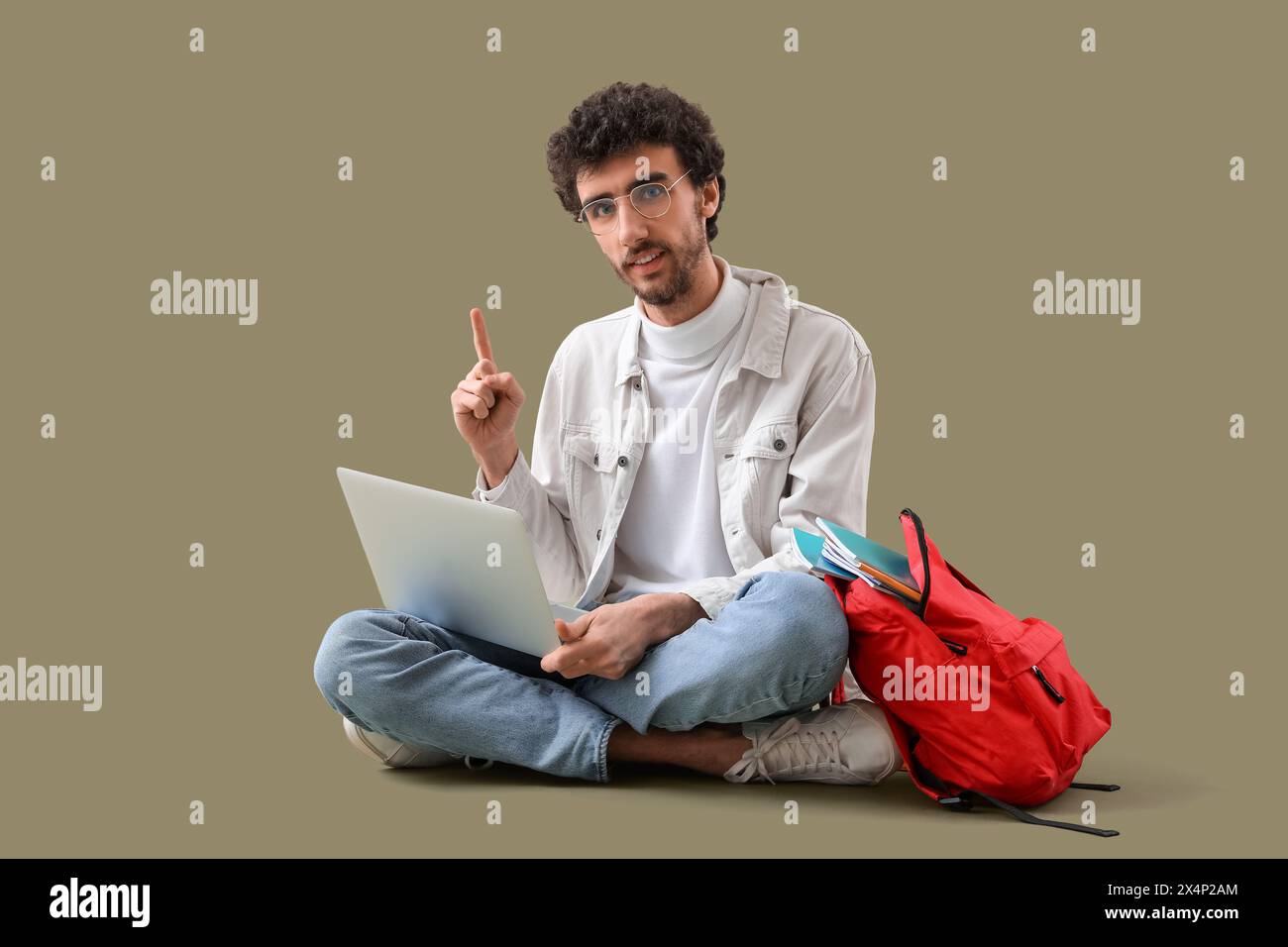Male student with laptop pointing at something on green background ...