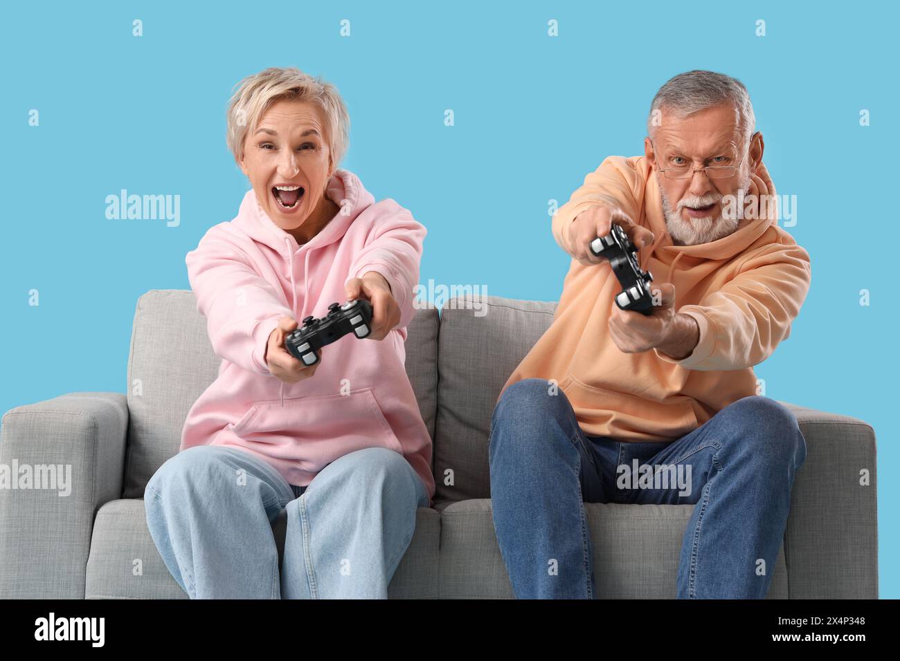 Mature couple playing video game on sofa against blue background Stock ...