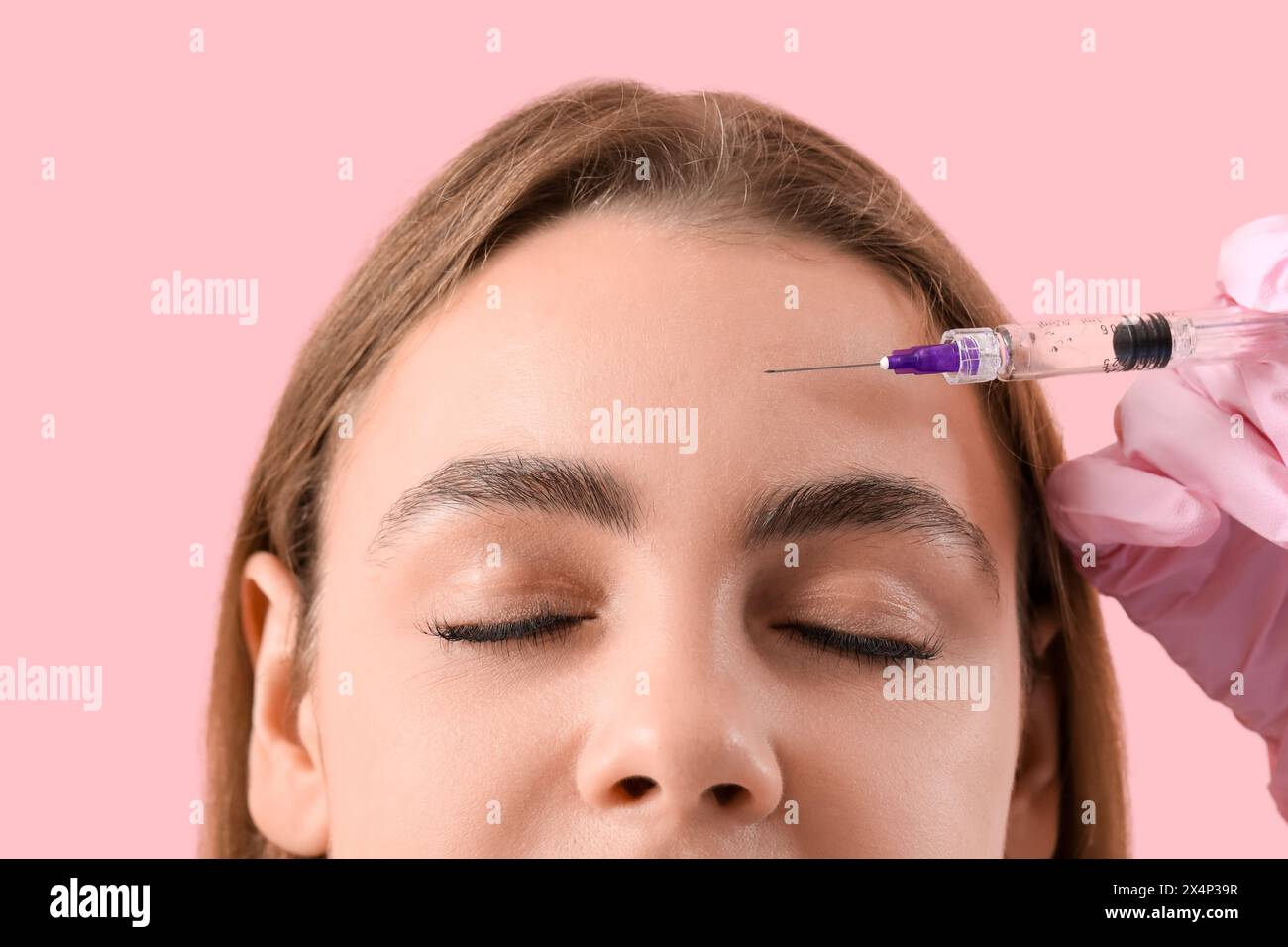 Young woman receiving filler injection in forehead on pink background ...