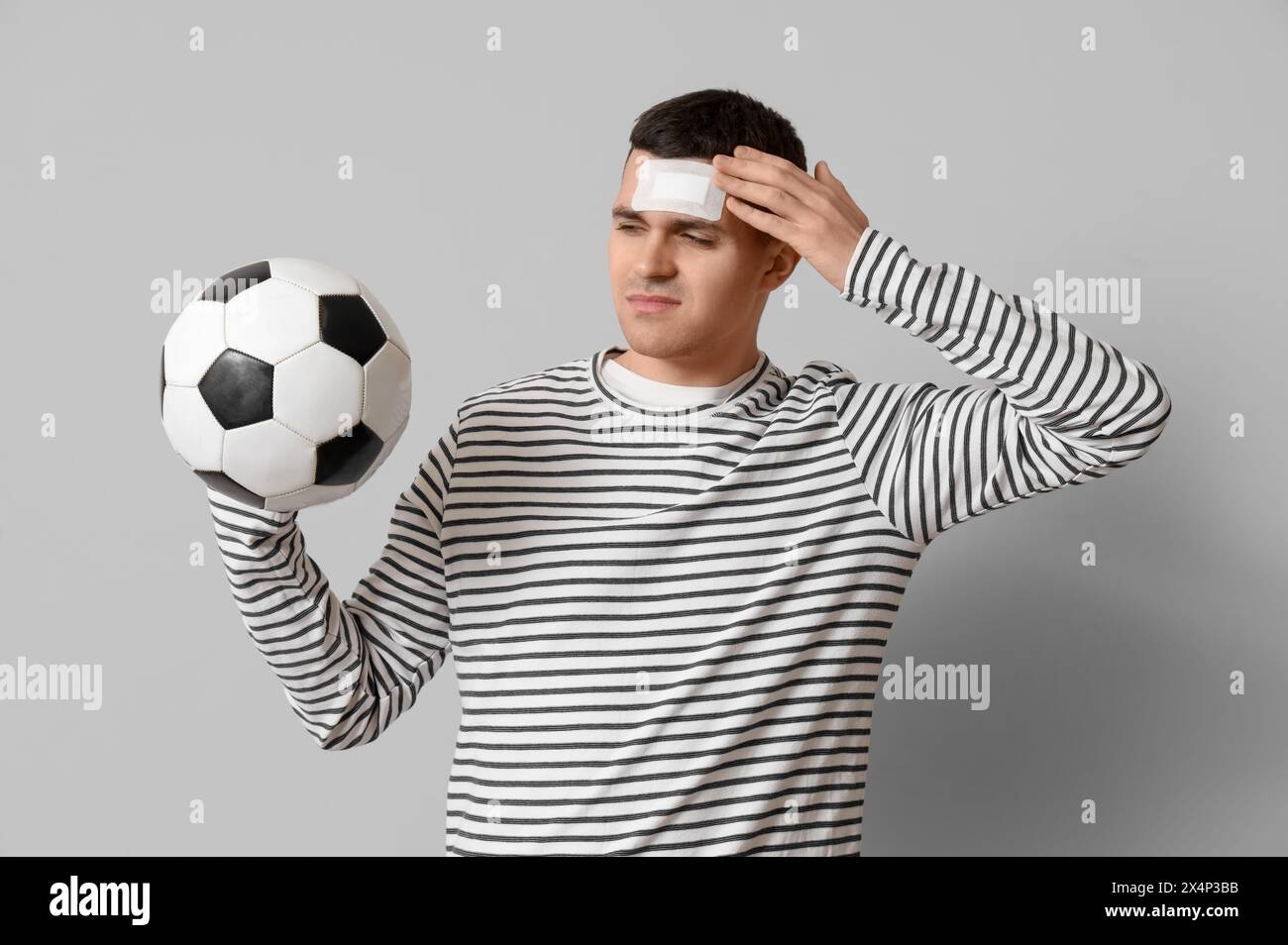 Young man with brain concussion and soccer ball on light background ...