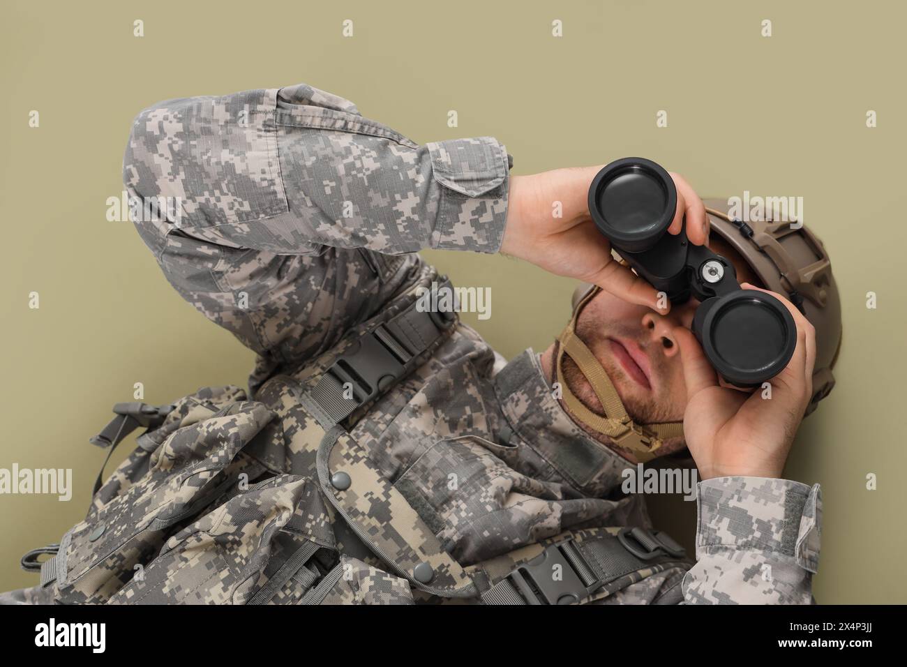 Lying male soldier in uniform looking through binoculars at something ...