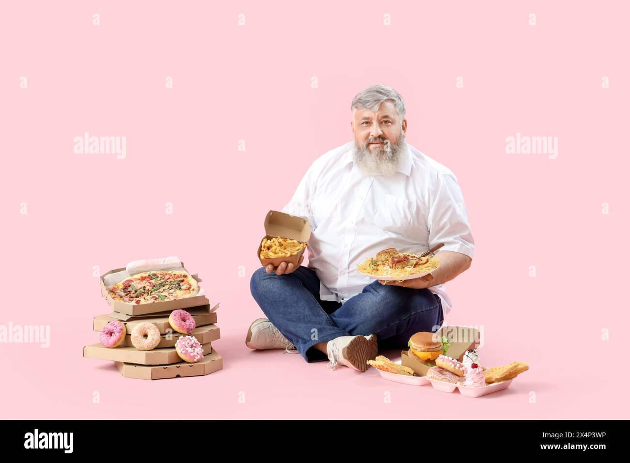 Overweight mature man with unhealthy food sitting on pink background ...
