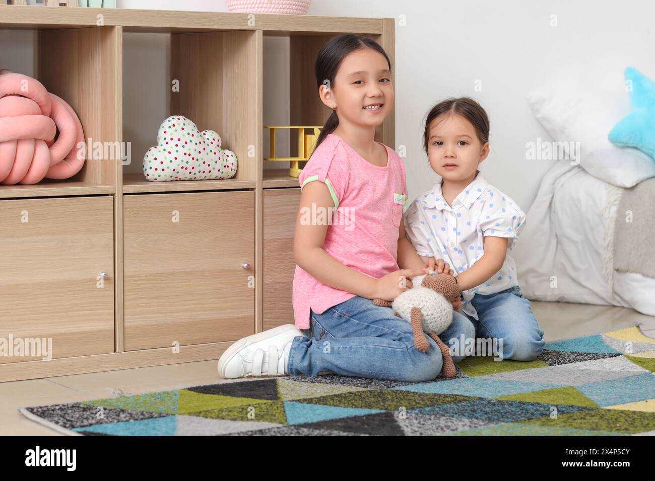 Cute little Asian happy sisters playing with plush sheep toy at child ...