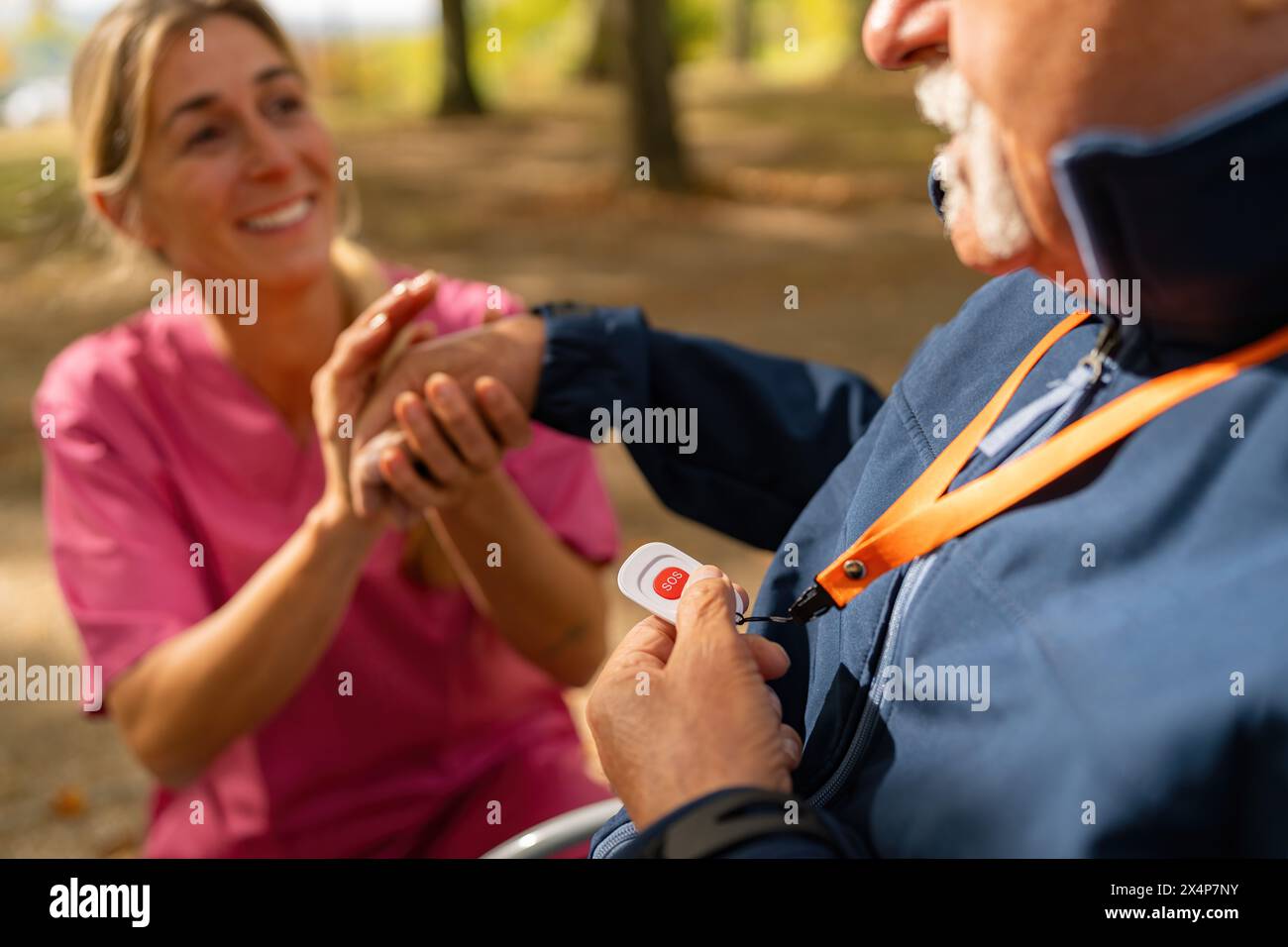 grandfather holding an SOS emergency button while a caregiver smiles at ...