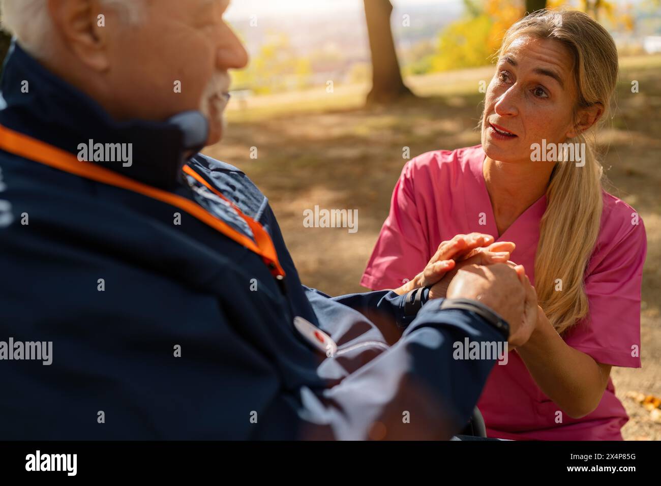 Caregiver holding hands with elderly man in wheelchair, conversation in ...